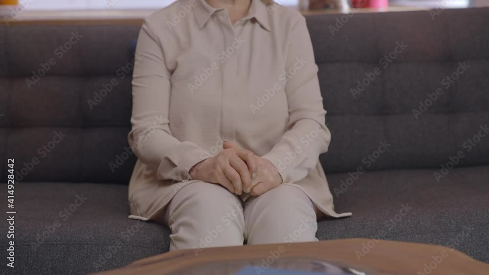 The old woman, sitting on the sofa, with her hands on her knees, joins ...