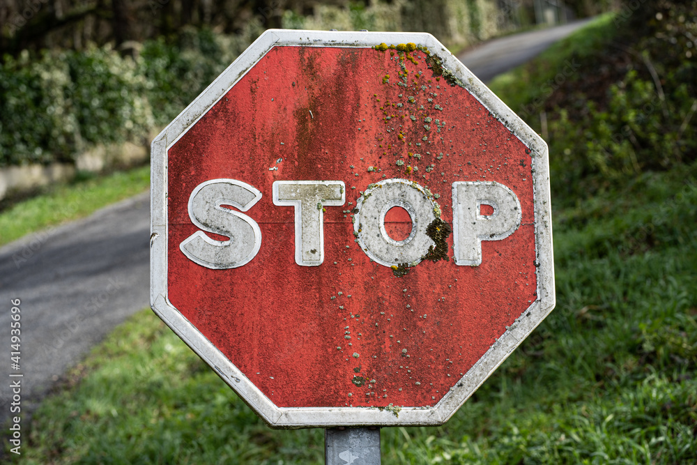Stop sign deteriorated by humidity and moss, with a road in the ...