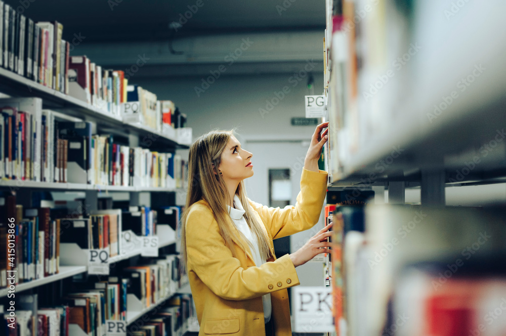 Beautiful girl student reads books in a library on the window sill ...