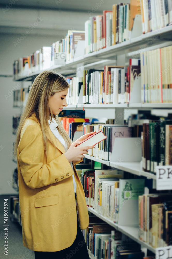 Beautiful girl student reads books in a library on the window sill ...
