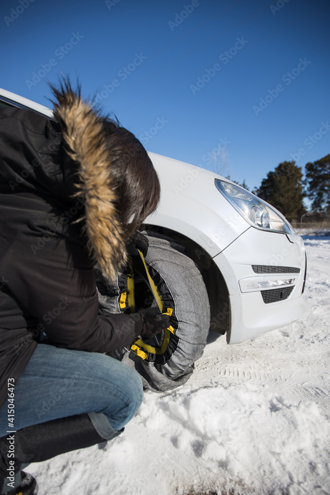 Side view of anonymous female driver changing wheel of car in winter ...