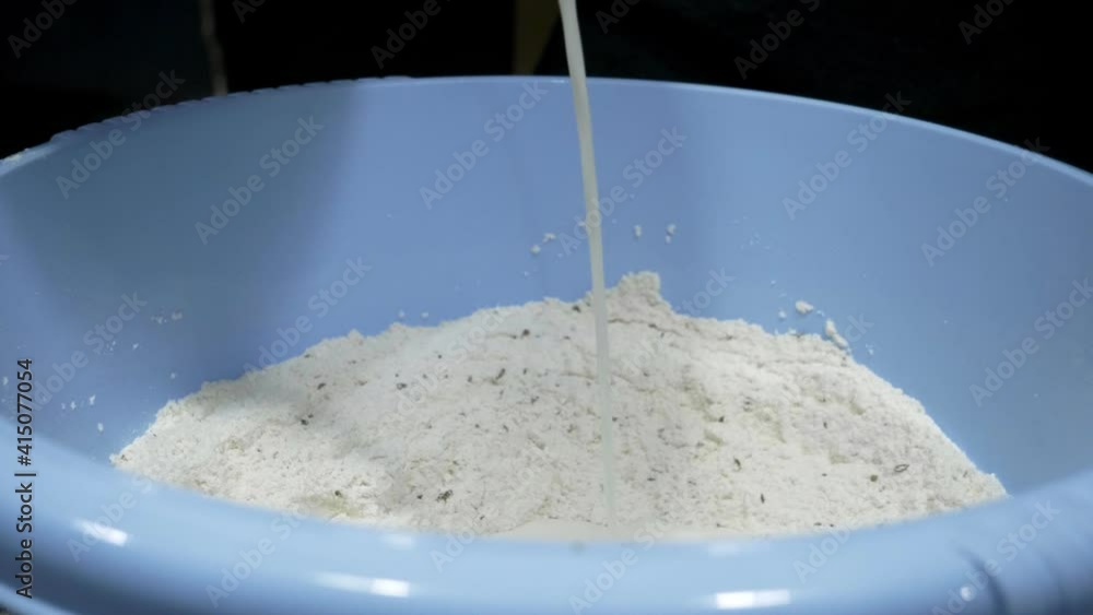 Milk is poured from jug into a blue bowl containing wheat flour and ...