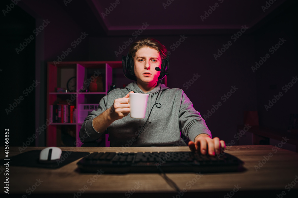 Handsome young male gamer sitting in a dark room with a purple saddle ...