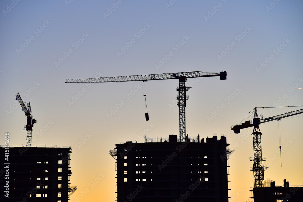 Tower cranes in action at construction site on sunset background. Crane ...