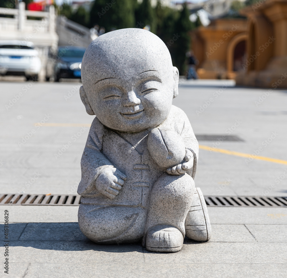 Stone figurine of little monk sitting on ground in courtyard of Qibao ...