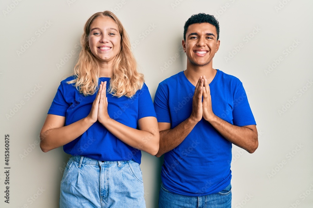 Young interracial couple wearing casual clothes praying with hands ...