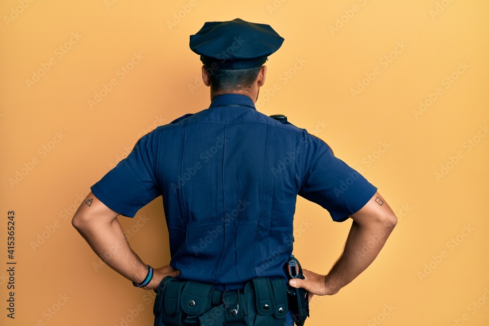 Handsome hispanic man wearing police uniform standing backwards looking ...