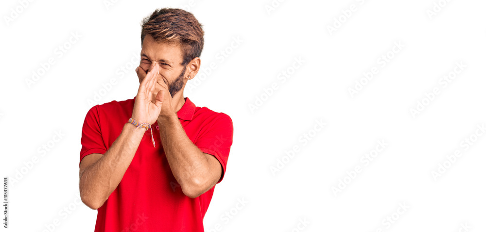 Handsome blond man with beard wearing casual clothes smelling something ...
