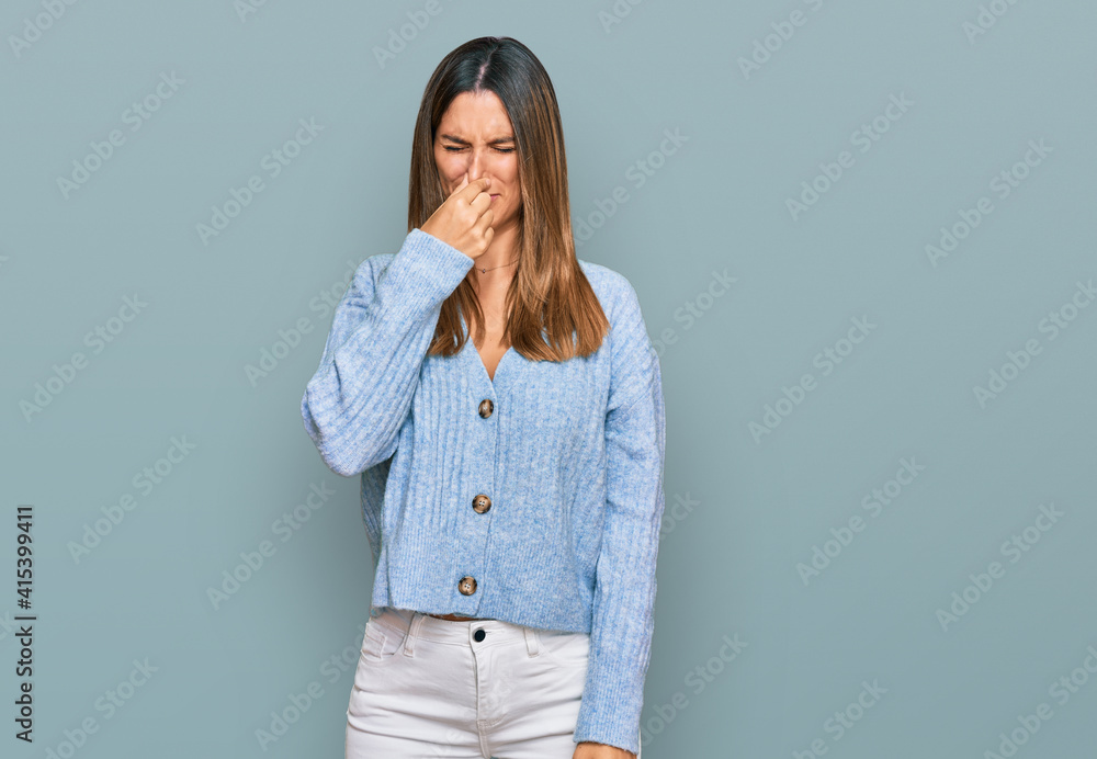 Young woman wearing casual clothes smelling something stinky and ...