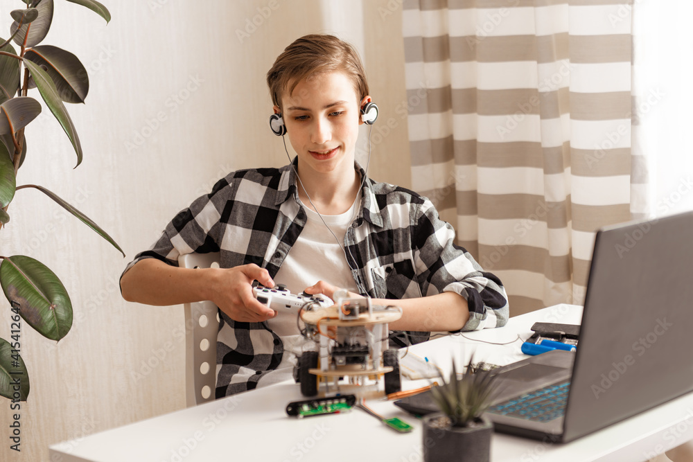Teen programming and plays science robotics project on his laptop at home during covid-19 ...