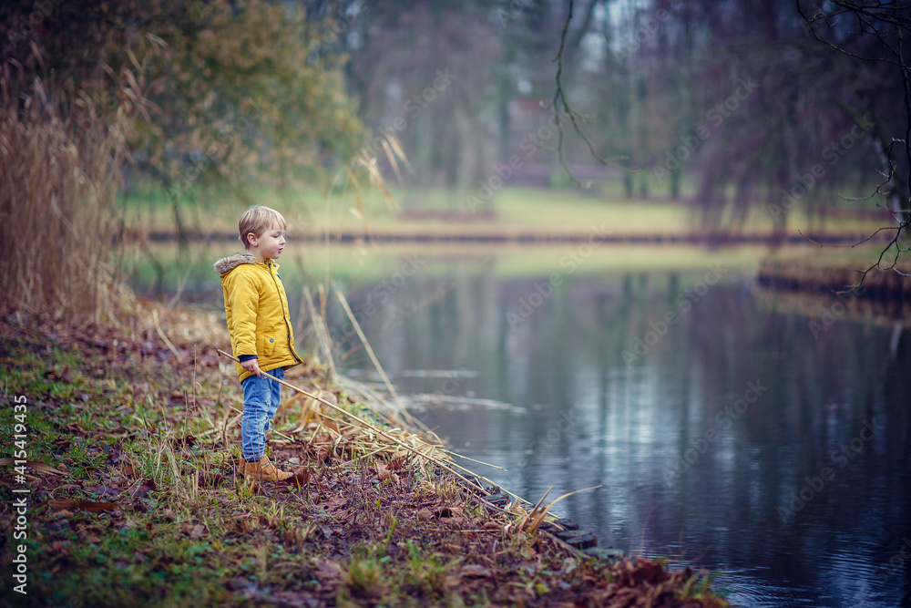 Little child trying to catch something with a long stick from a lake ...