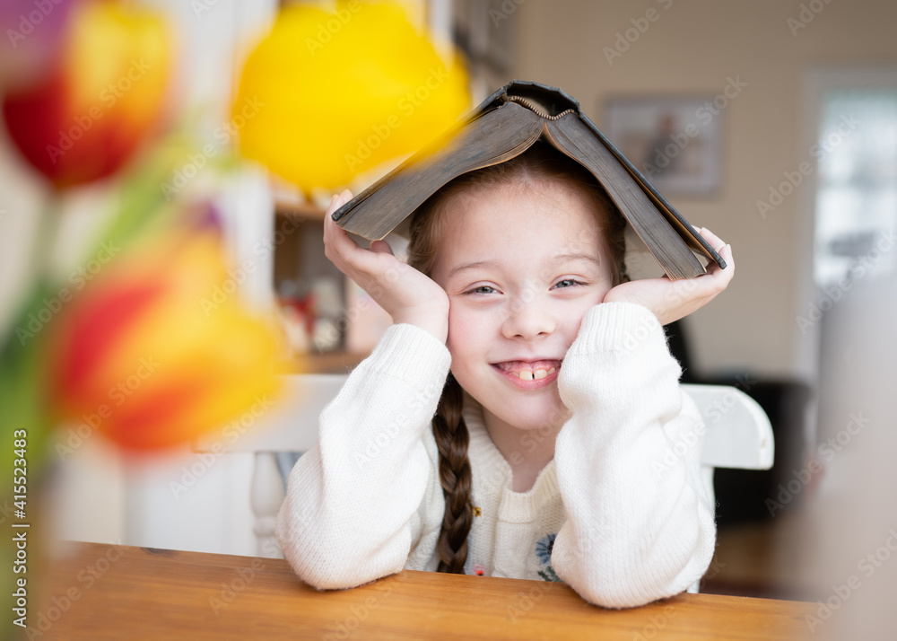 Beautiful happy young girl lockdown homeschooling with big book having ...