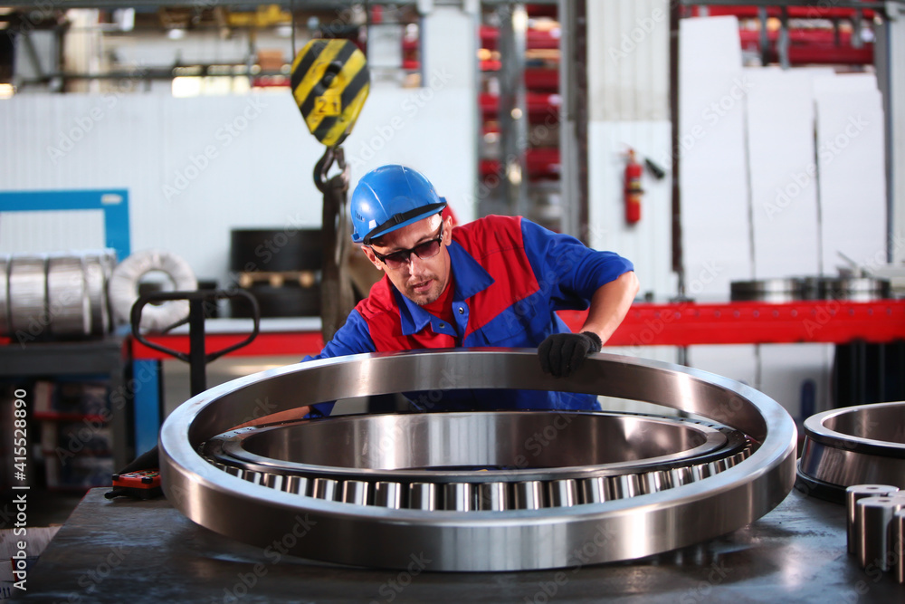 The worker moves a large diameter bearing. Bearing plant. The ...