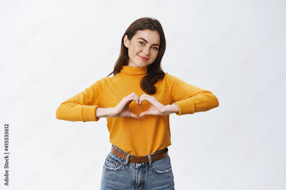 Cute female model smiling, showing hand heart gesture over chest and ...