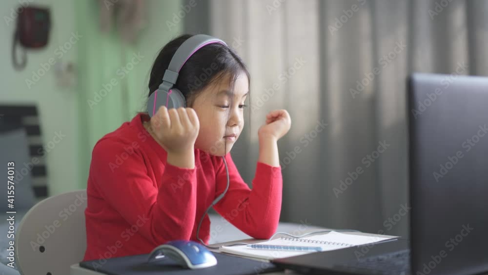 Asian child student or kid girl smile e-learning on computer notebook to wearing headphone for ...