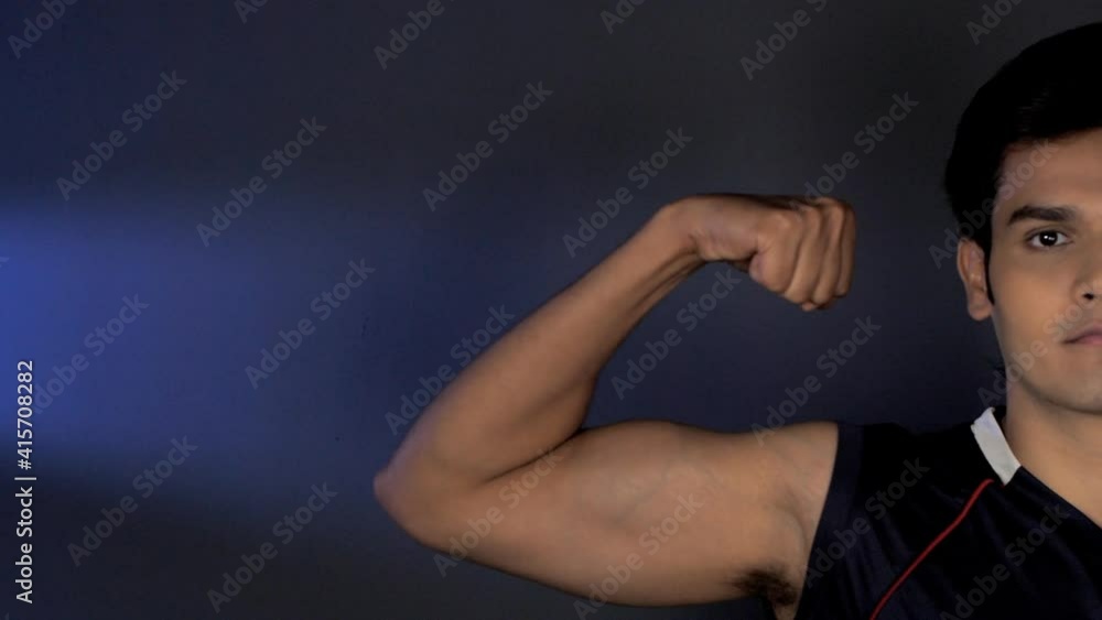 Half face of healthy Indian male showing his biceps against a dark ...