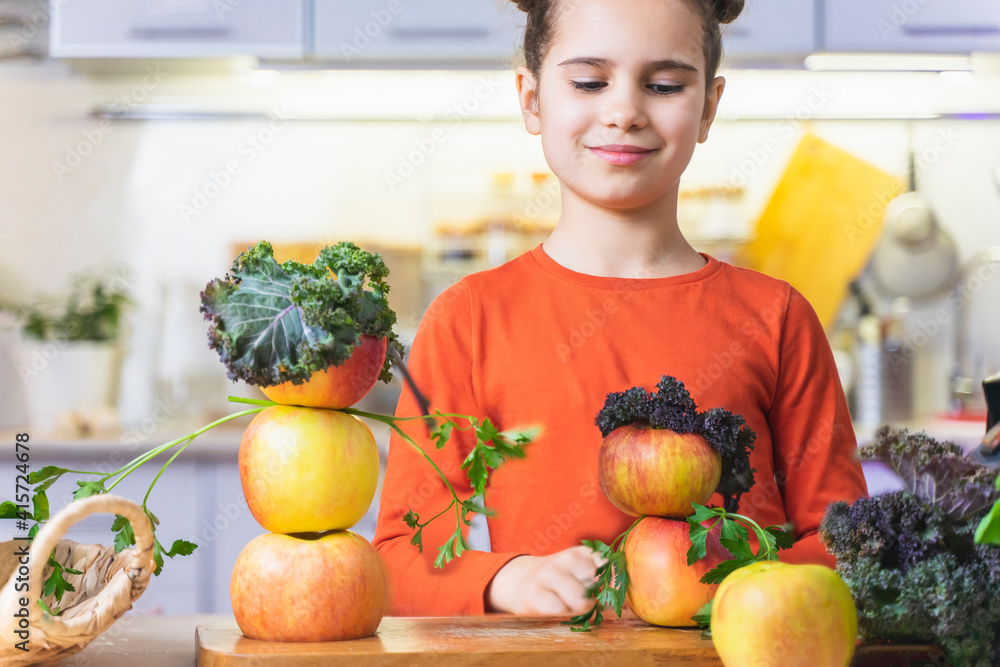 Funny kid building pyramid of apples in kitchen, crazy having fun. Girl ...