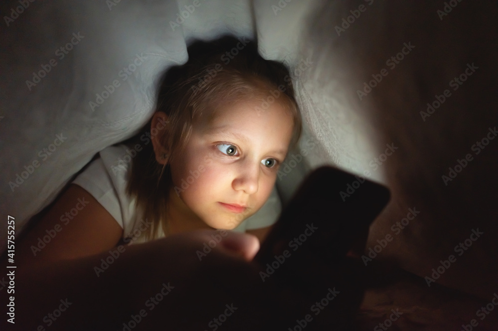 Foto de Child watching video smartphone under the blanket on the bed at ...