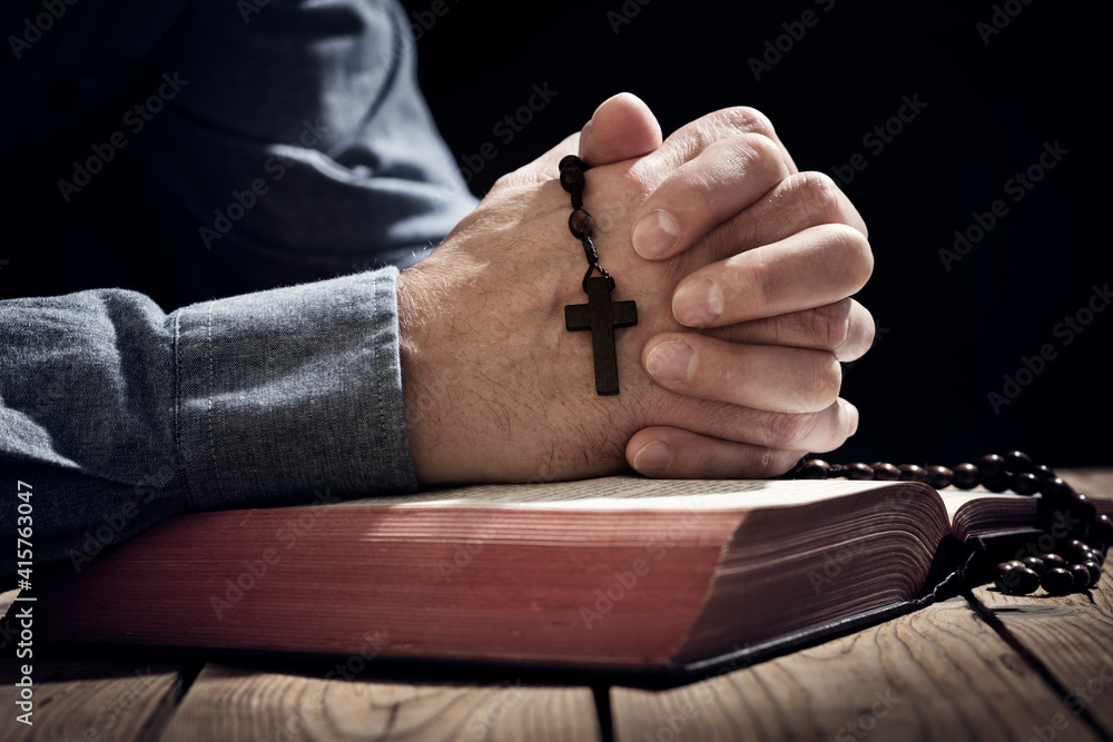 Praying hands on a Holy Bible with religious cross and rosary beads ...