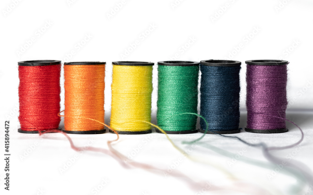 Unwinding spools of thread in colors of the rainbow on white background ...