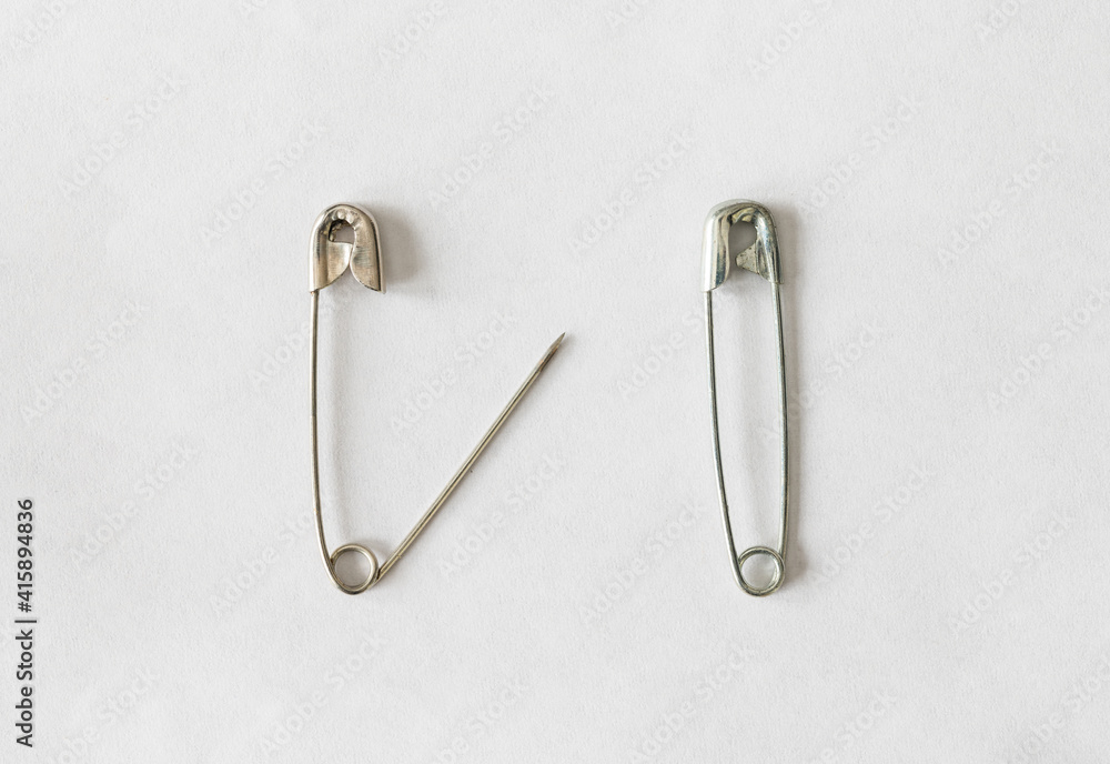 Two silver safety pins on white background, open safety pin on left, closed safety pin on right ...