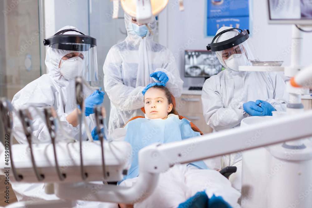 Mother dressed in ppe suit comforting daughter in the course of dental ...