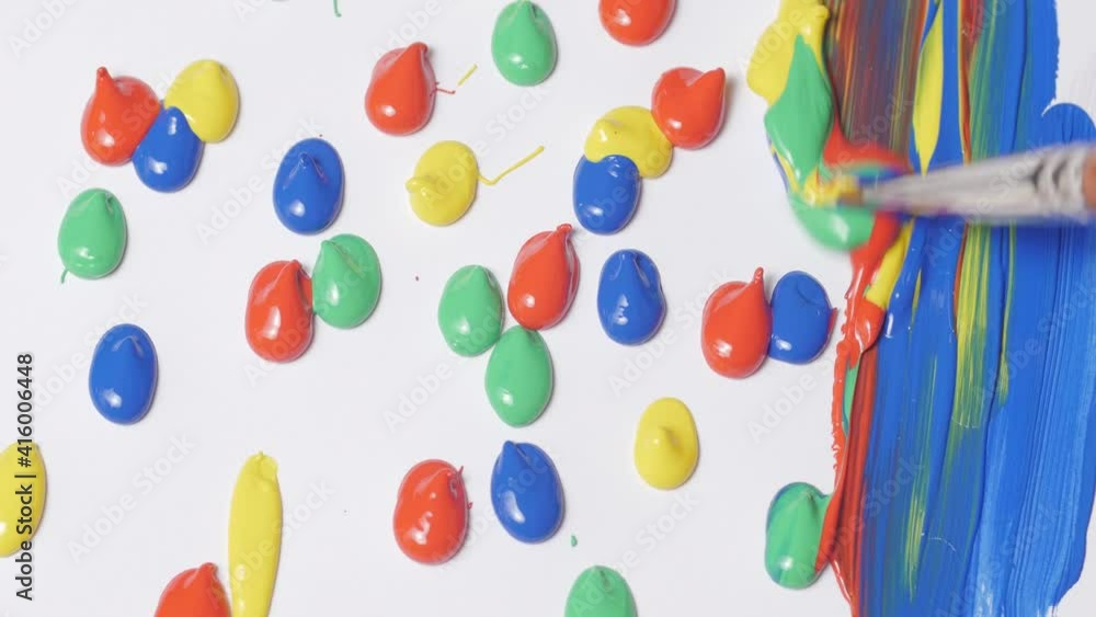 dots of colored paint mixing into one color with brush on white ...