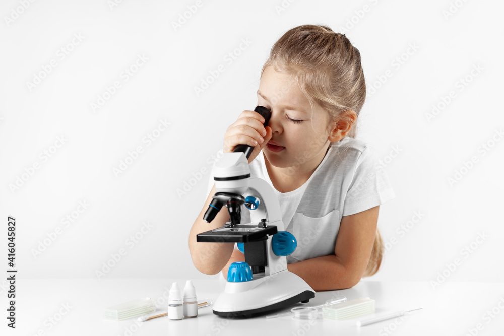 Interested child girl looks through a microscope on a white background ...