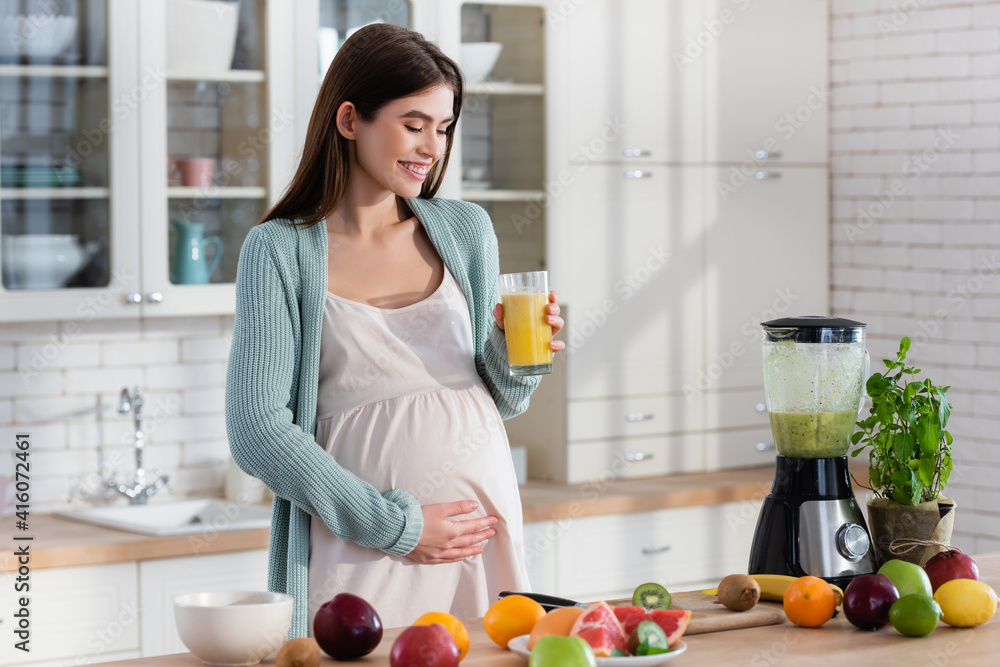 Happy Pregnant Woman Touching Tummy While Holding Fresh Juice In