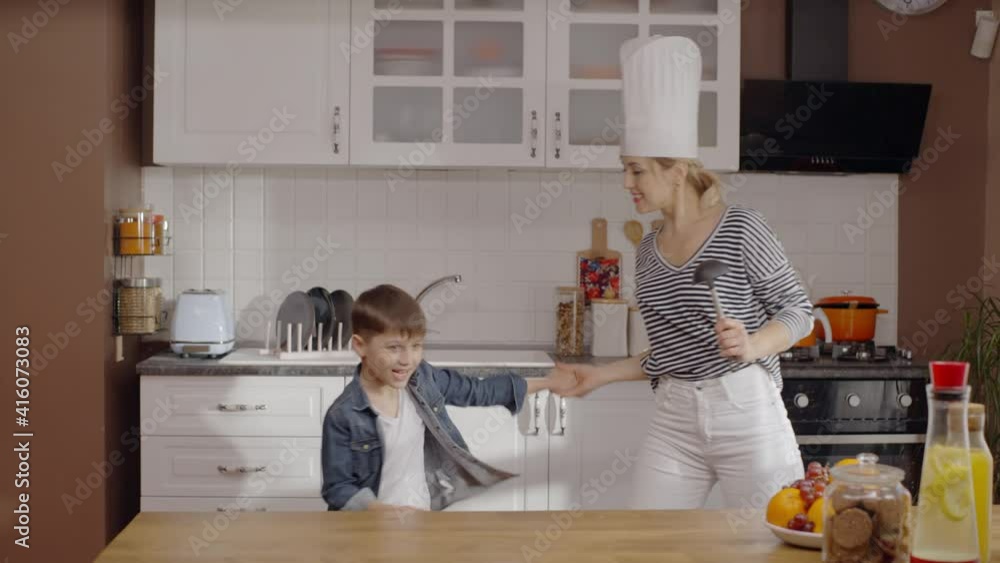 Young mom and son wearing chef hats dance in the kitchen, sing with a ...