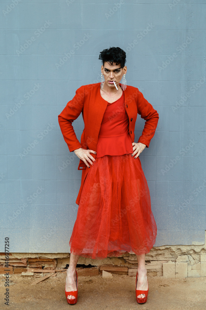 Transgender woman in red clothing, posing and smoking, with an wall of ...