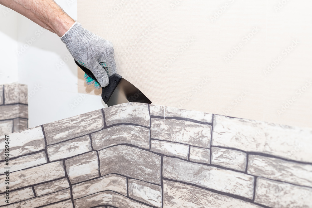 Man hand tear off old light wallpaper from wall.Preparing for home ...