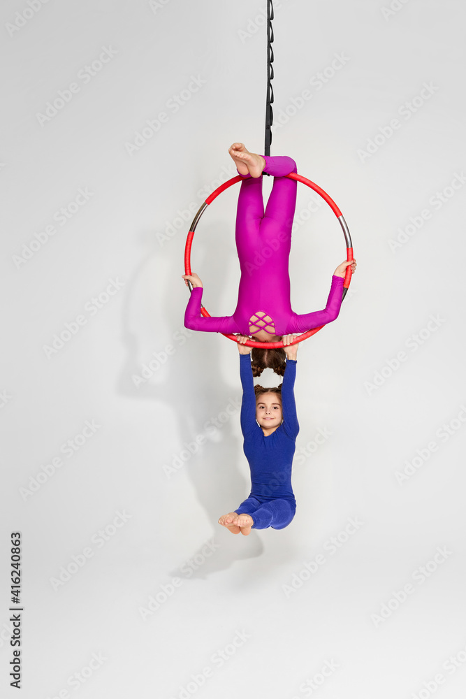 two little child girls shows an acrobatic performance on an aerial hoop ...