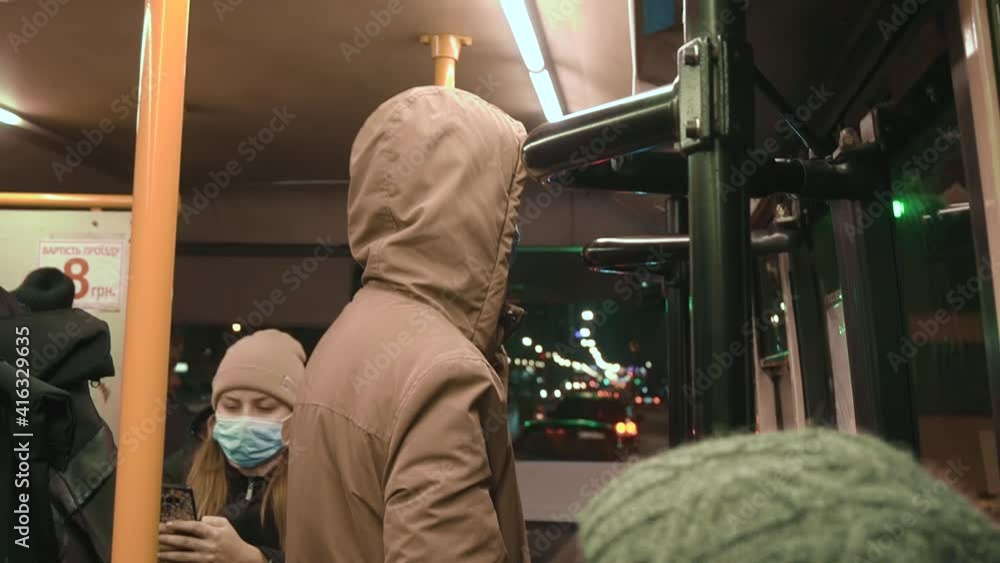 man in jacket and hood stands in moving public transport wearing mask ...
