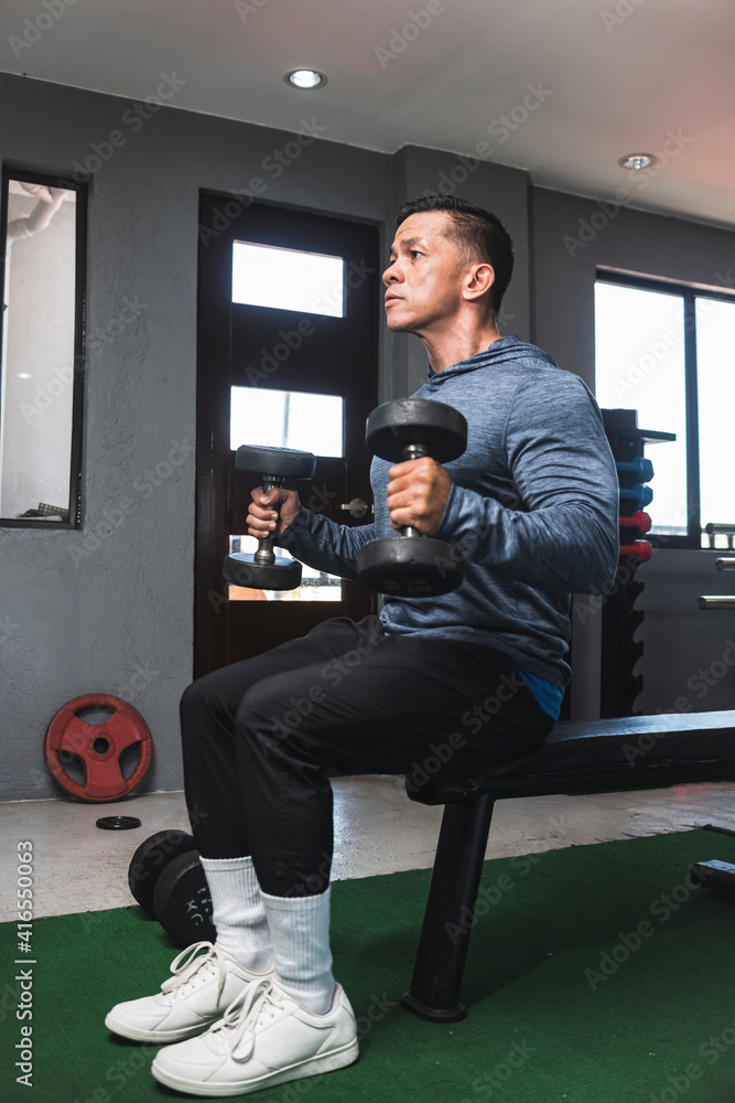 A fit athletic guy in a sweatshirt does seated dumbbell hammer curls ...