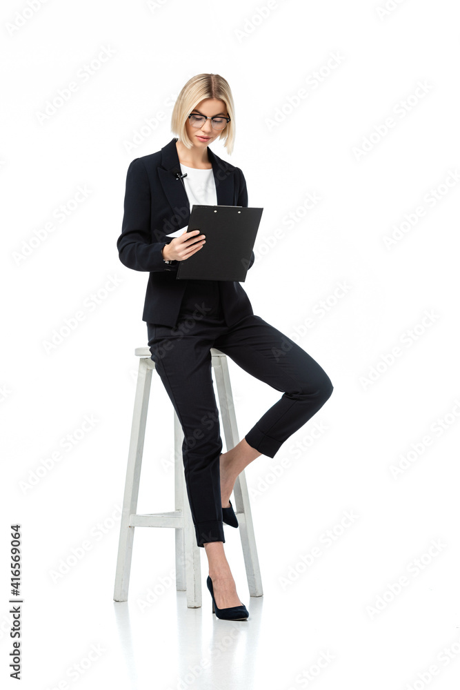 full length view of news anchor sitting on high stool with clipboard on ...