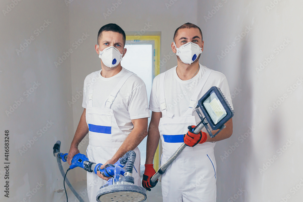 Plasterer smoothes the wall surface with a wall grinder. Two master ...