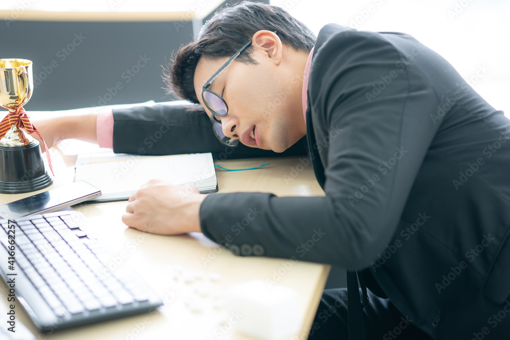 Tired asian young man sleeping on work desk in office. Lazy employee ...