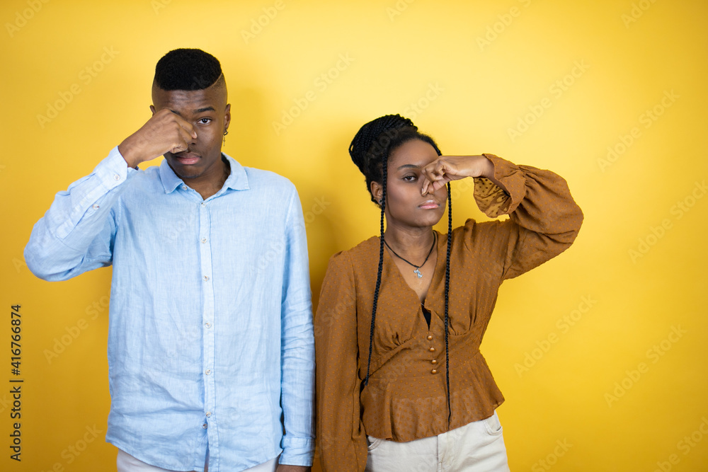 Young african american couple standing over yellow background smelling ...