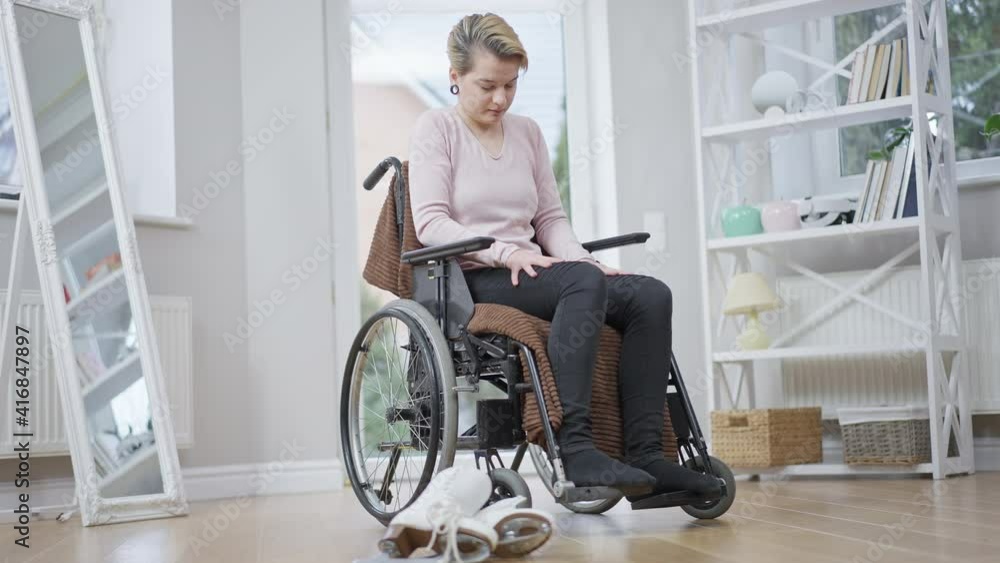 Sad frustrated woman in wheelchair rubbing paralyzed legs as ice skates ...