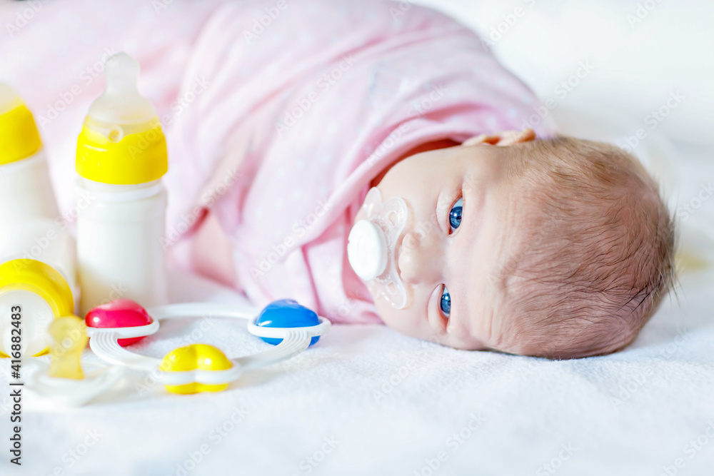 Cute newborn baby girl with nursing bottles, rattle and pacifier ...