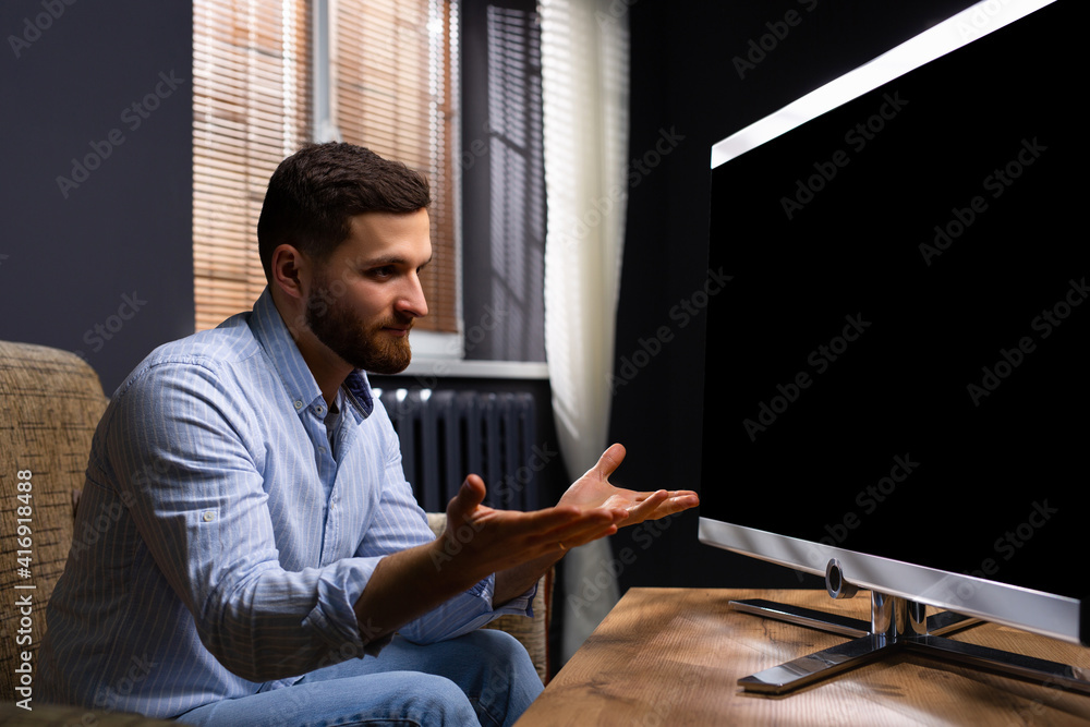 Outraged man at home sitting on the couch in front of a large TV screen ...