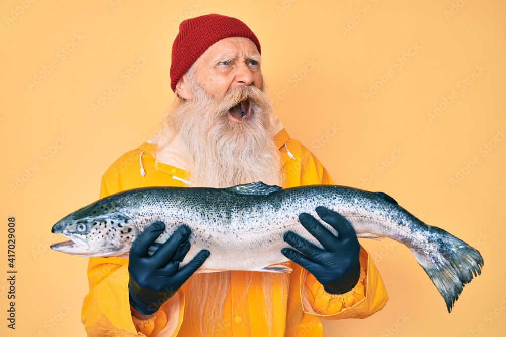 Old senior man with grey hair and long beard wearing raincoat holding ...