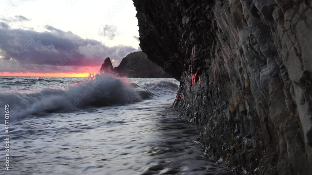 Colorful warm sunset over the sea and volcanic basalt rocks, like in ...