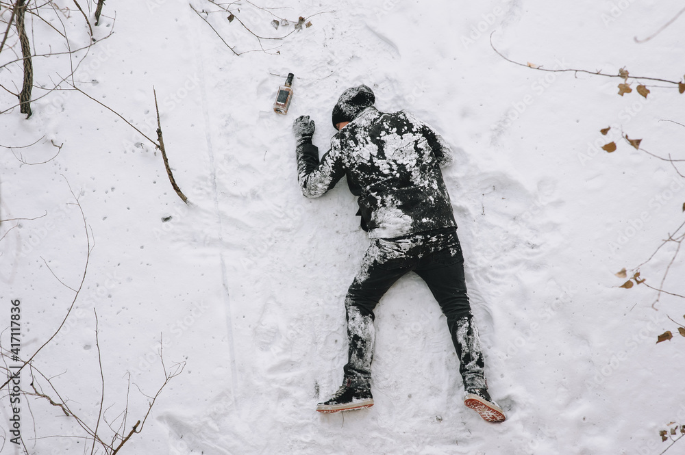 A very drunk homeless and dirty unconscious man in a black coat lies ...