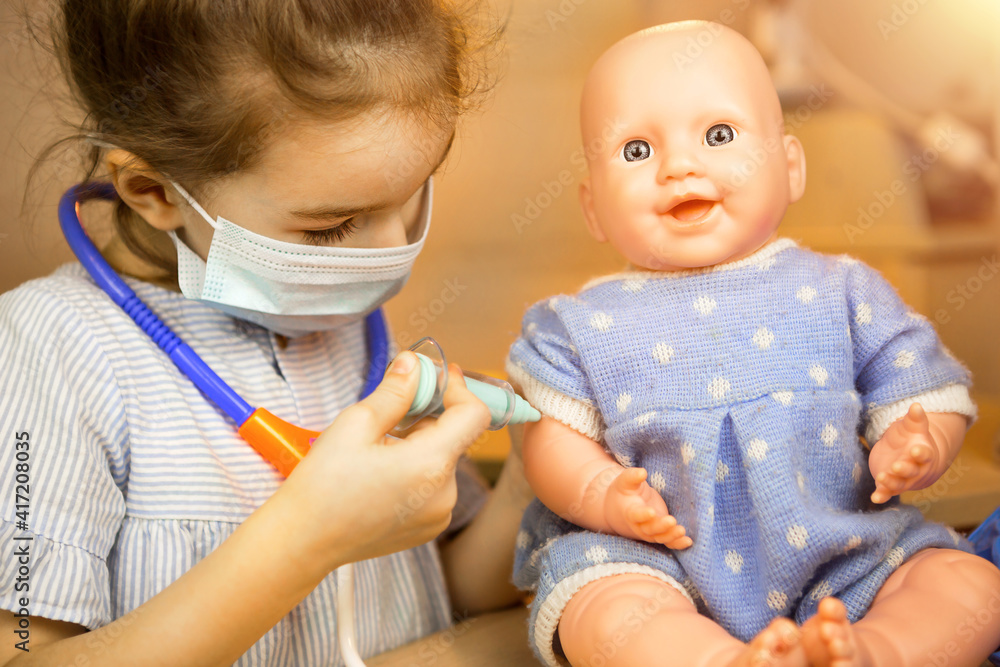 A girl with a doll plays doctor, makes a syringe inoculation in the ...