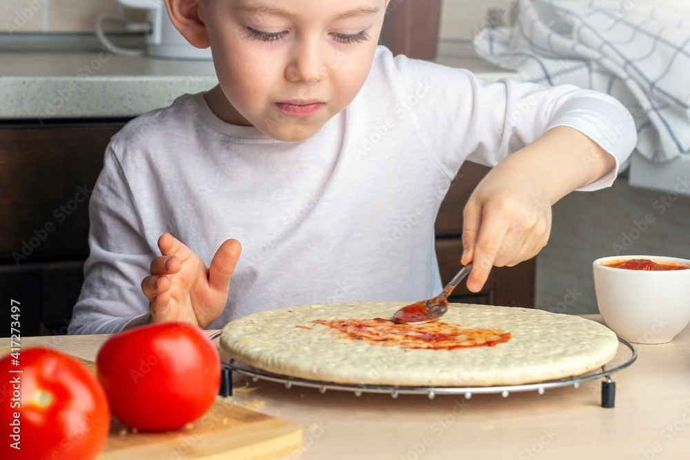 Kid spreads the sauce on pizza dough. Process of cooking homemade pizza ...