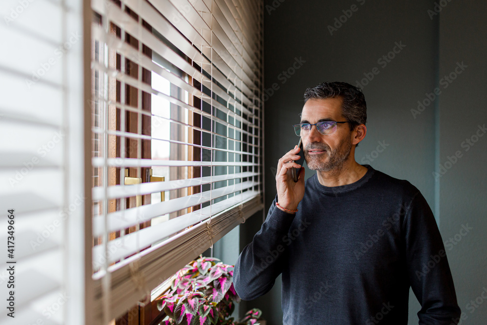 Man talking on the phone while looking out the window of his house ...