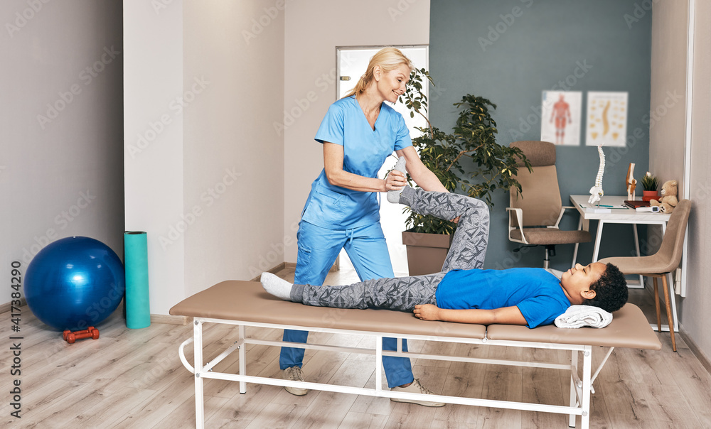 Foto de Physiotherapist treating leg injury on a little boy lying down ...