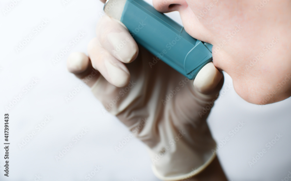 A woman uses an inhaler during an asthma attack. Using a blue asthma ...